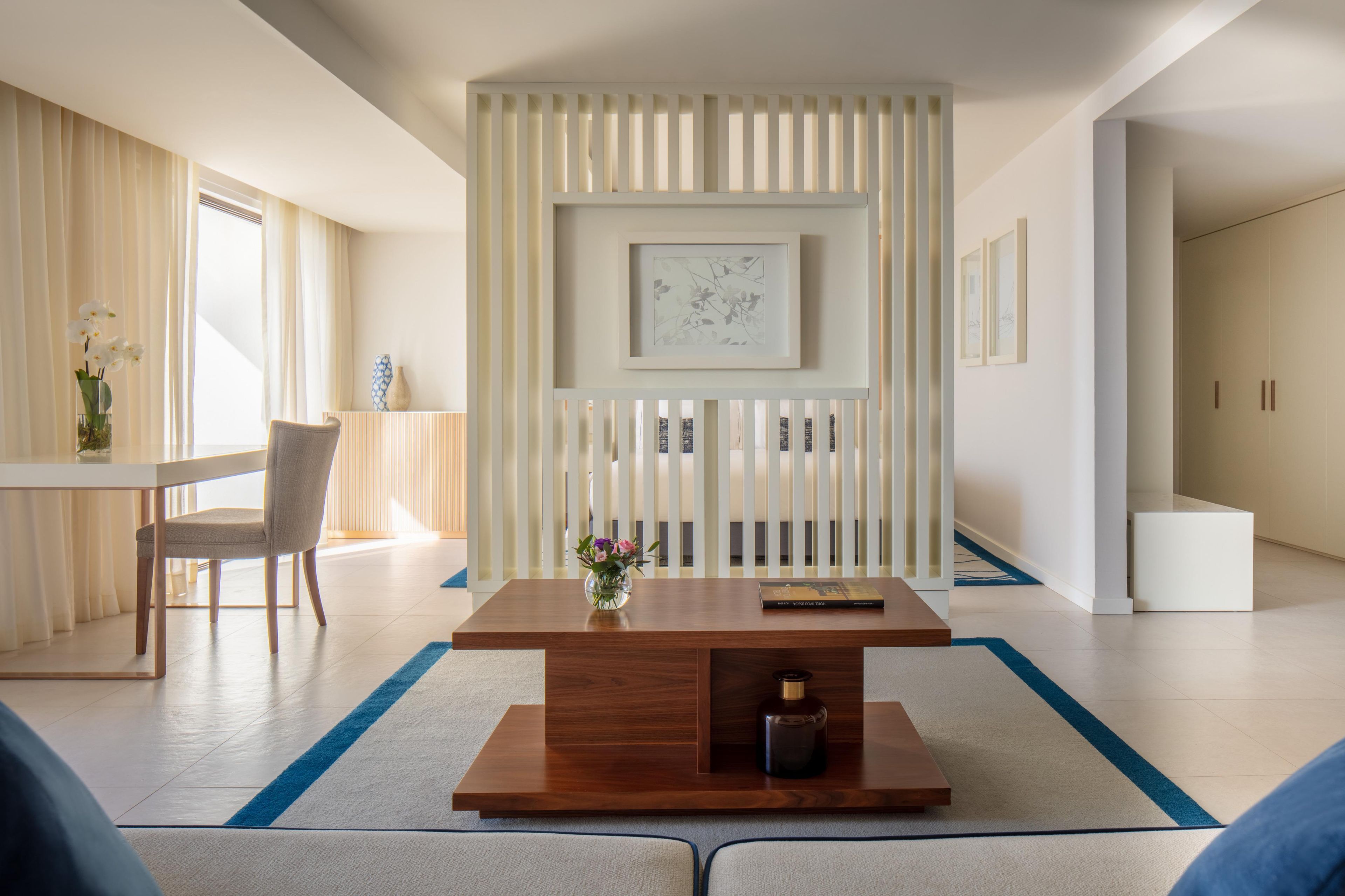 Uma sala de estar moderna com uma mesa de centro de madeira, um sofá, uma área de refeições com uma cadeira e um painel decorativo com ripas verticais.