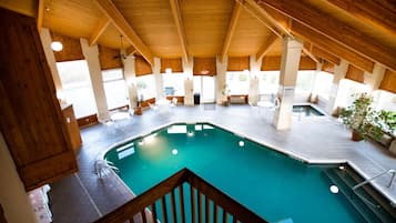 Piscina interna com vigas de madeira, piso cerâmico e área com bancos.