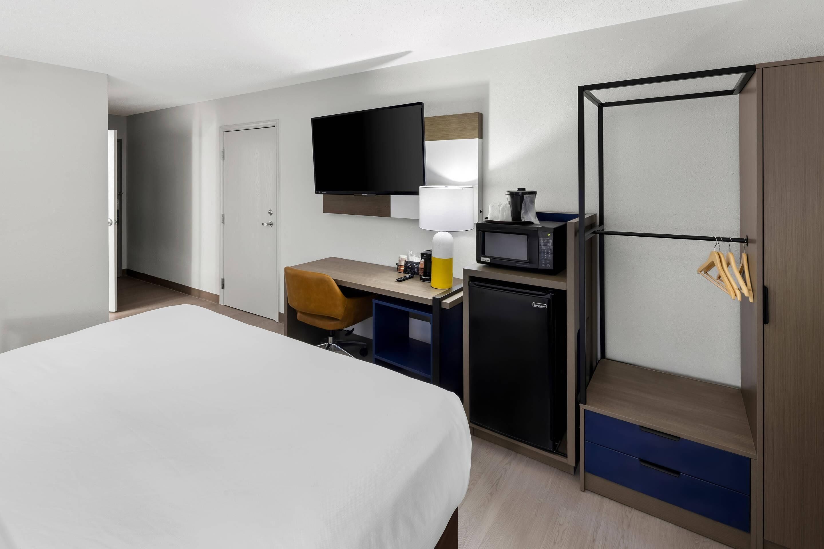 Quarto de hotel com cama, escrivaninha, micro-ondas, televisão e guarda-roupa.