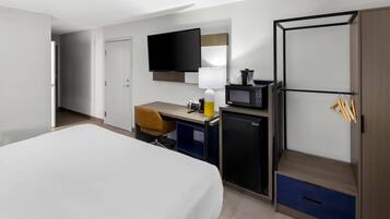 Quarto de hotel com cama, escrivaninha, micro-ondas, televisão e guarda-roupa.