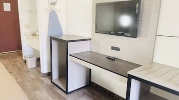 Quarto de hotel moderno com televisão de tela plana na parede, uma pequena mesa com cadeira e uma lixeira.