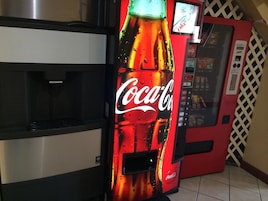 Máquina automática com logotipo da Coca-Cola, visor digital e abertura para moedas.