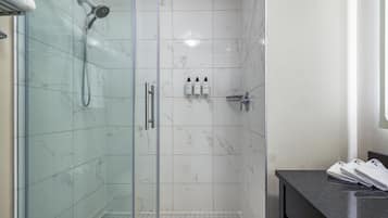 Casa de banho moderna com cabine de chuveiro em vidro, azulejos de mármore branco e bancada preta com toalhas.