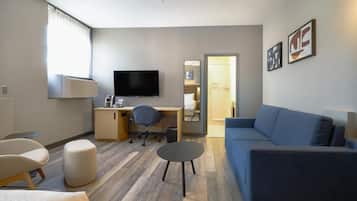 Quarto de hotel com cama, escrivaninha, poltrona, sofá, televisão e espelho.