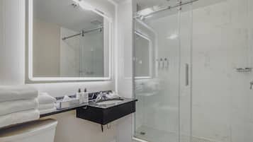 Uma casa de banho moderna com chuveiro em cabine de vidro, um espelho grande e bancada preta com produtos de higiene pessoal.