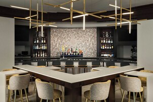 Uma área de bar com balcão central, diversas opções de assento e parede decorativa com padrão em mosaico.