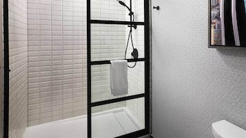 Uma casa de banho moderna com cabine de duche em vidro, paredes com azulejos brancos e sanita branca.