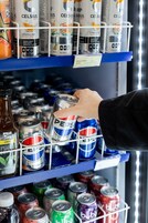 Mão selecionando uma lata em um refrigerador de bebidas.