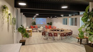 Uma sala de conferências moderna com uma mesa redonda, cadeiras vermelhas e plantas em vasos.