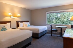 Quarto de hotel com duas camas, uma mesinha e uma cadeira.