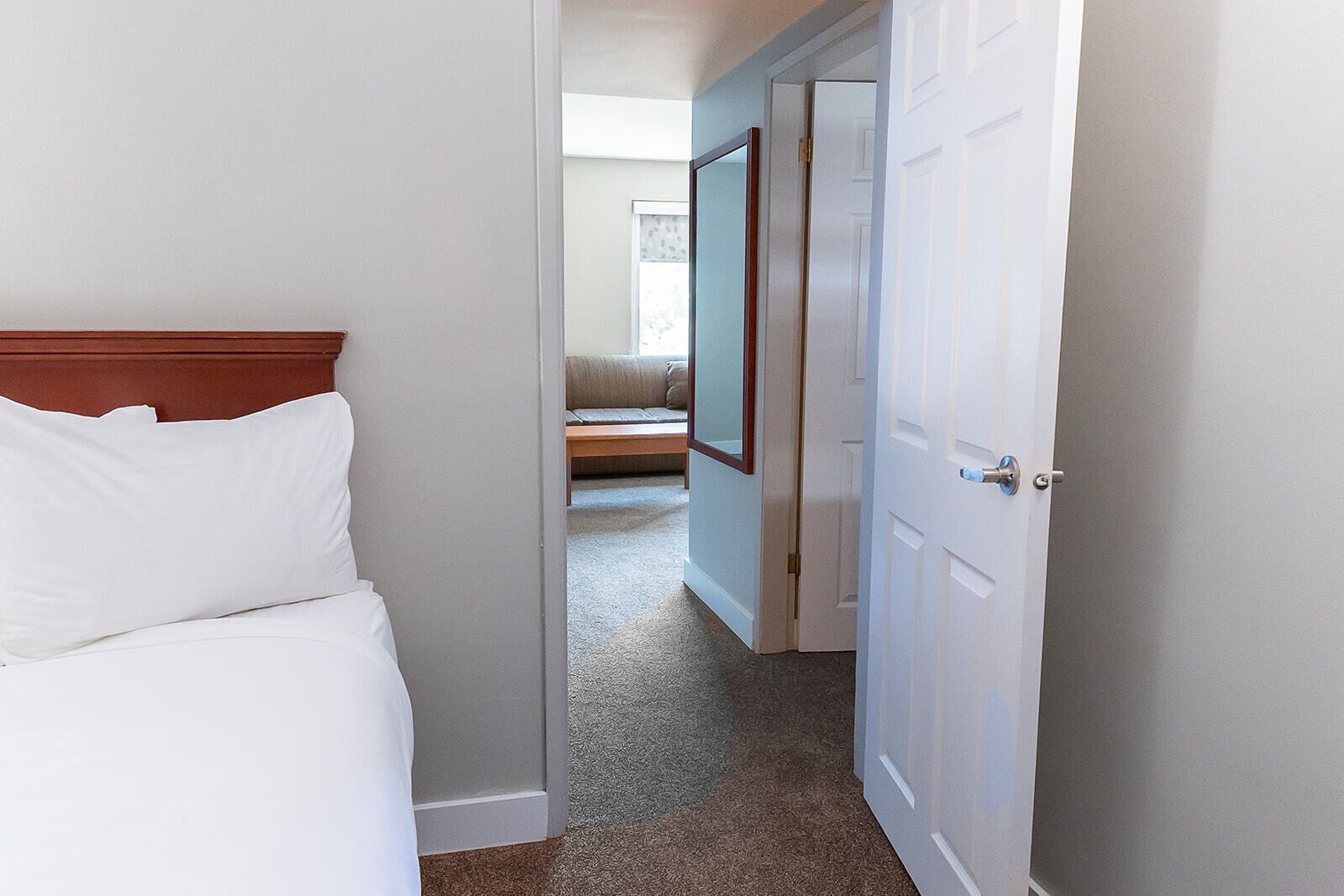 Quarto de hotel com uma cama, uma porta que dá para outro cômodo e piso coberto por carpete.