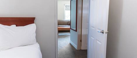 Quarto de hotel com uma cama, uma porta que dá para outro cômodo e piso coberto por carpete.