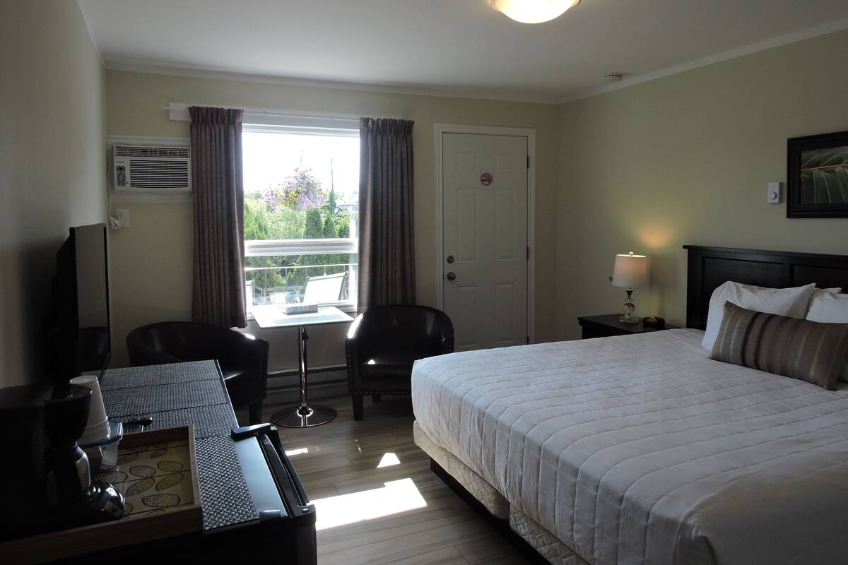 Quarto de hotel com cama, escrivaninha com computador, cadeira, janela com cortinas e luminária no teto.