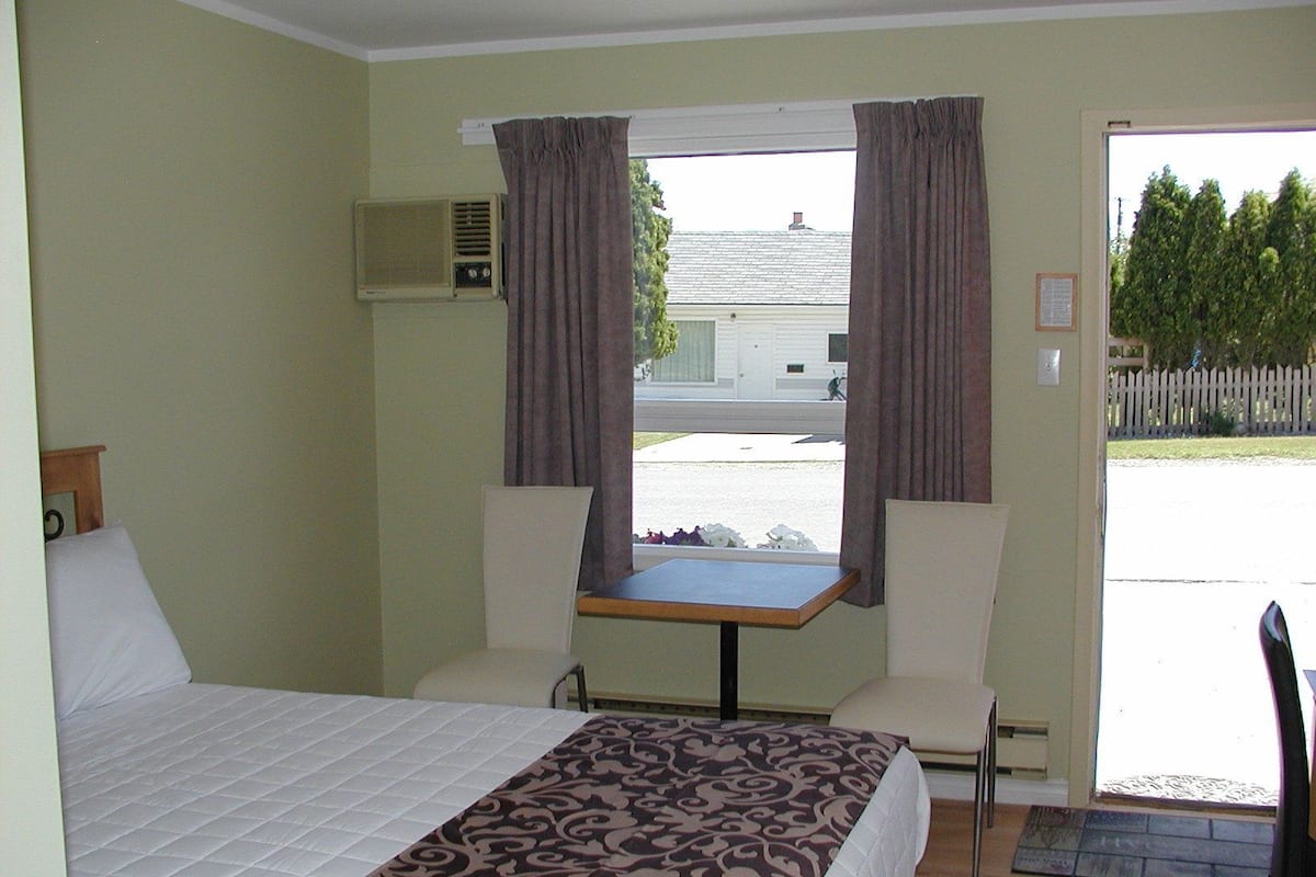 Quarto com cama, uma mesinha, duas cadeiras e janela com cortinas.