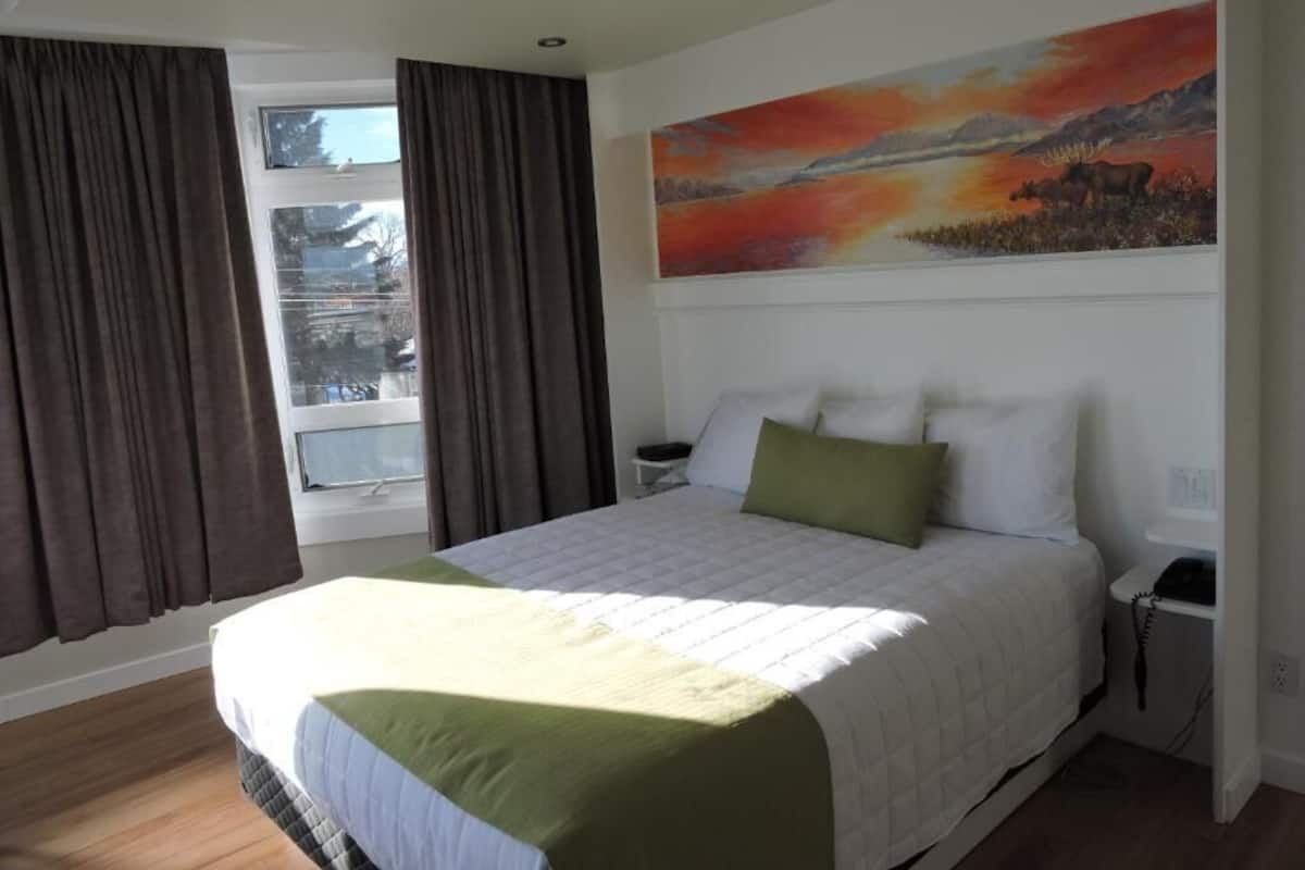 Quarto de hotel com uma cama grande, um quadro de pôr do sol, uma janela com cortinas e uma mesa de cabeceira.