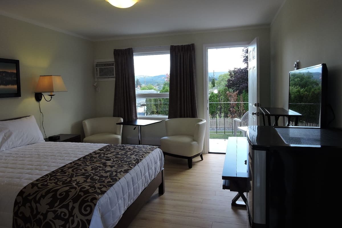 Quarto de hotel com uma cama, duas cadeiras, uma mesa pequena, uma escrivaninha, uma TV e uma varanda com vista.