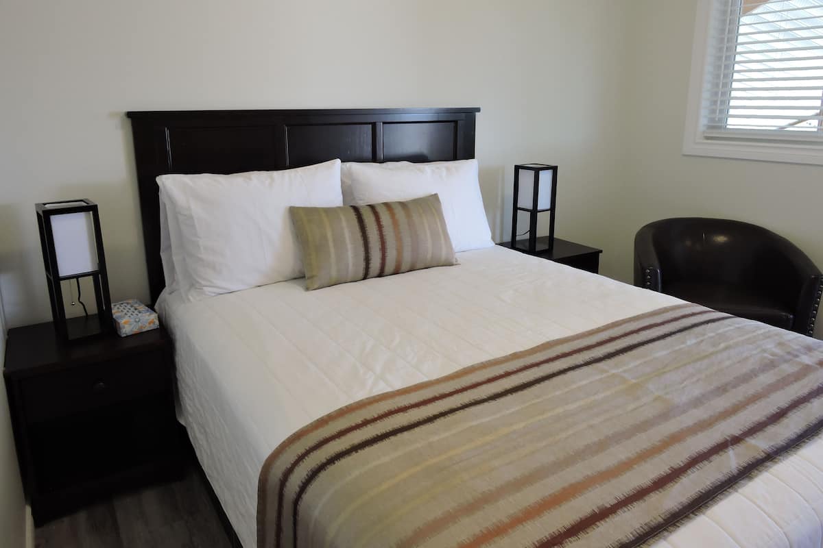 Cama bem arrumada com manta listrada, cabeceira escura e duas mesas de cabeceira com abajures.