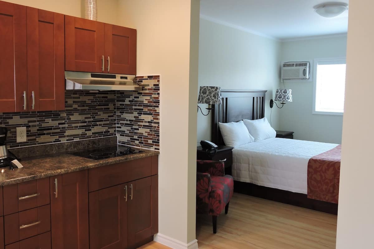 Quarto de hotel compacto com cozinha compacta, cama com roupa de cama branca, mesa de cabeceira e janela com ar condicionado.