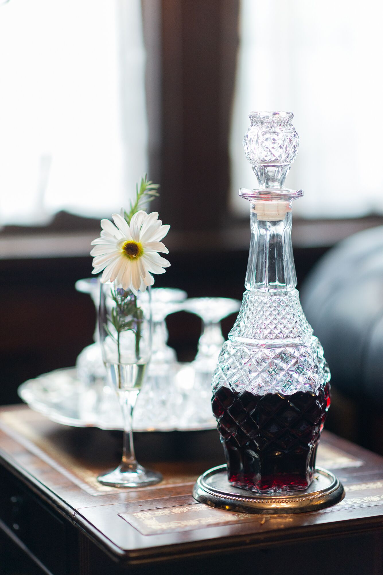 Um jarro de cristal e um vaso de vidro com uma margarida sobre uma mesa de madeira.