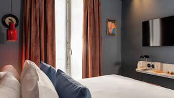 Quarto de hotel com cama, cortinas, relógio, quadro, televisão e escrivaninha com abajur e placa.