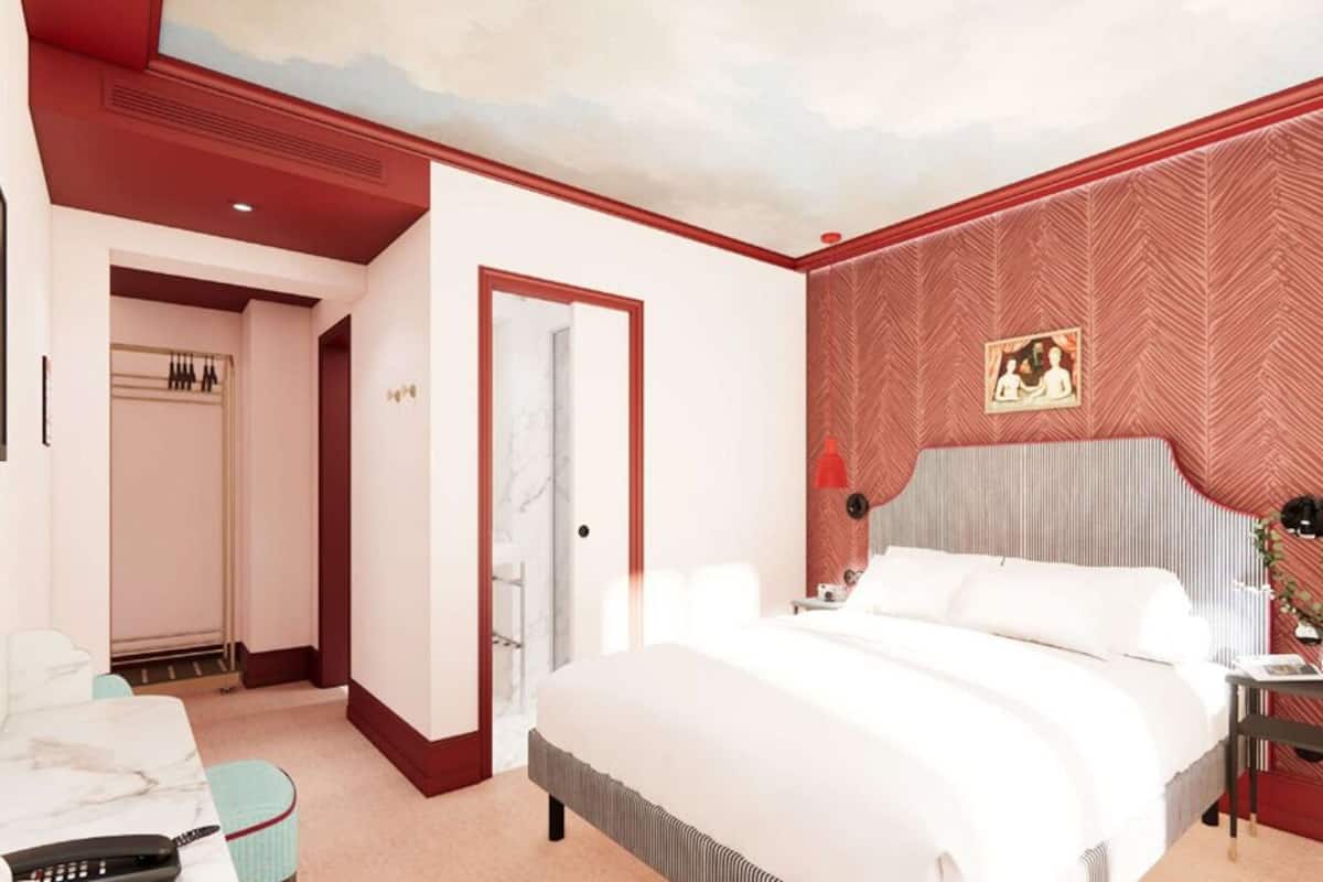 Quarto de hotel com cama, mesa de cabeceira e espelho. Há uma porta que dá para o banheiro.