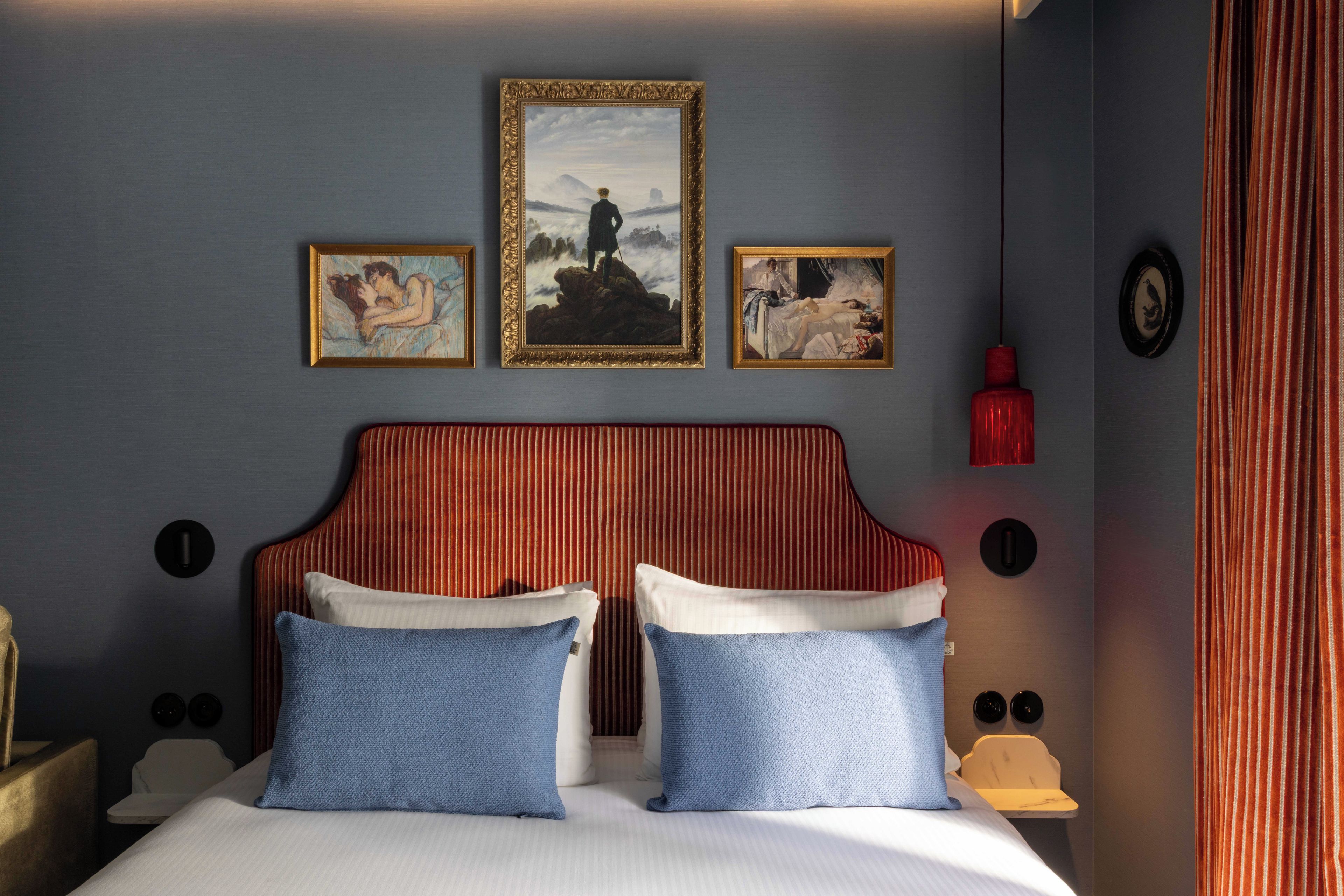 Quarto de hotel com cama grande, duas almofadas, cabeceira e três obras de arte emolduradas na parede.
