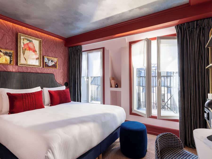 Quarto de hotel com uma cama grande, varanda com cortinas e obras de arte na parede.