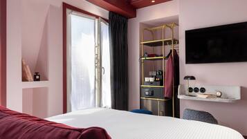 Quarto de hotel com cama, televisão na parede, escrivaninha com computador e janela com cortinas.