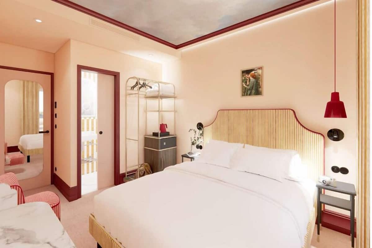 Quarto de hotel com uma cama grande, mesa de cabeceira, espelho, guarda-roupa e uma luminária pendente vermelha.