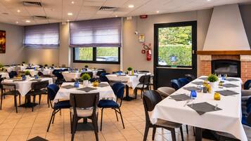 Uma sala de jantar com várias mesas preparadas para hóspedes, com cadeiras e louças.