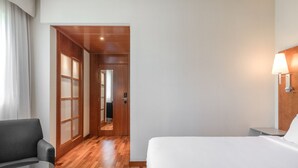 Quarto de hotel com cama, escrivaninha, cadeira e guarda-roupa de madeira.