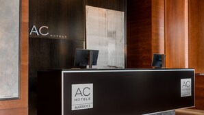 Uma receção com a marca AC Hotels Marriott, uma grande obra de arte abstrata na parede e um painel de madeira.