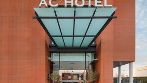 Exterior de um hotel AC com design moderno, apresentando uma entrada de vidro e um céu claro ao fundo.