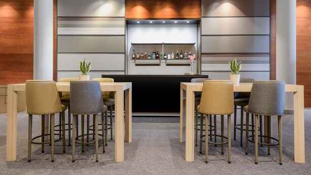Uma área de jantar moderna com bar, apresentando uma mesa comprida com seis cadeiras, bancada preta com diversos frascos e duas plantas em vasos.