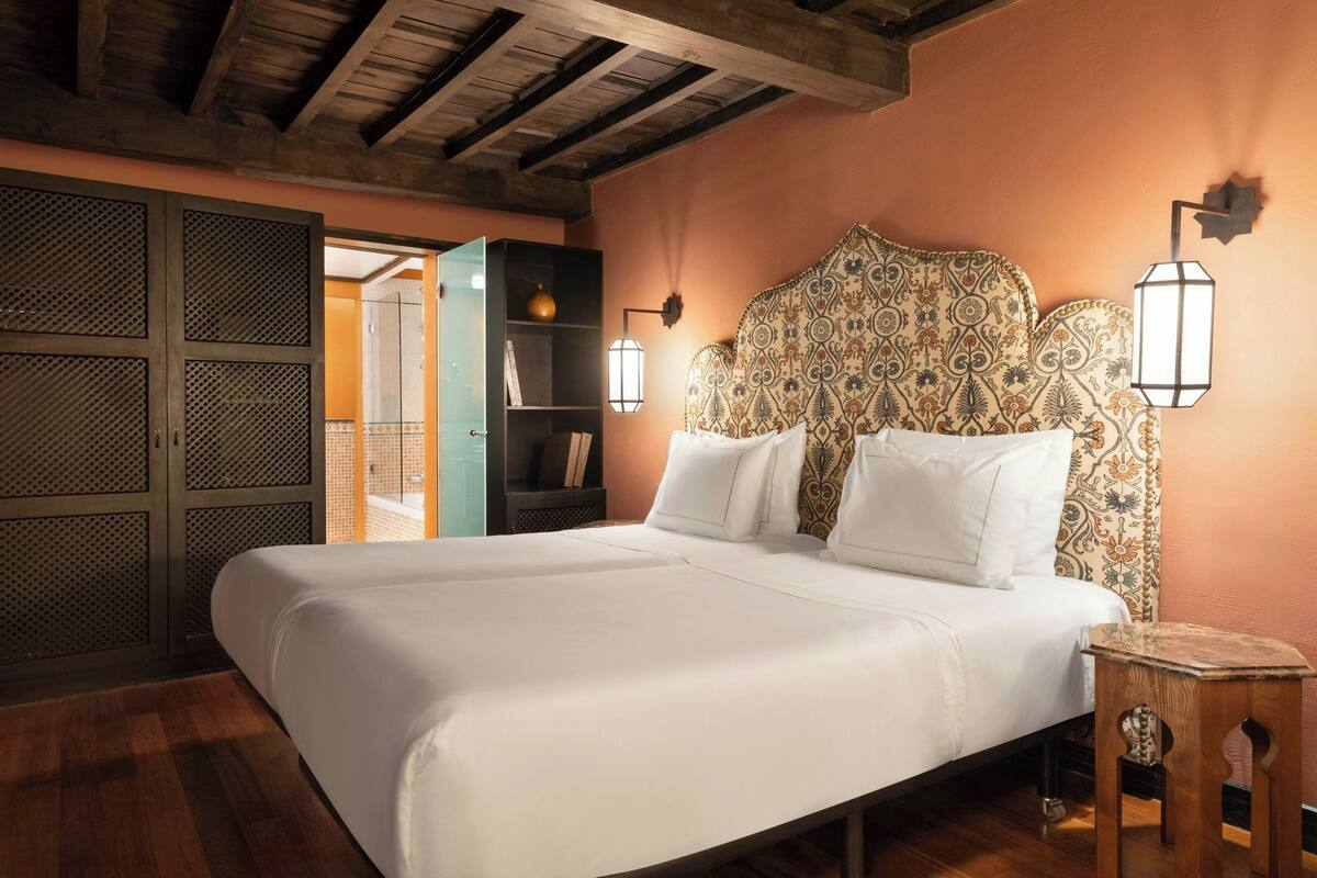 Uma cama grande com cabeceira estampada, mesa de cabeceira de madeira e uma estante.