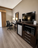 Quarto de hotel com escrivaninha, cadeira, televisão, mini-geladeira e micro-ondas.