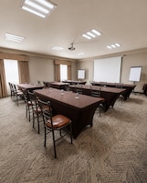 Sala de conferência com várias mesas, cadeiras, tela de projetor e lousa.