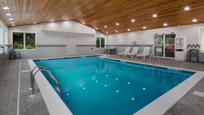 Piscina com teto de madeira e paredes revestidas de azulejos, cercada por espreguiçadeiras e uma porta de vidro.
