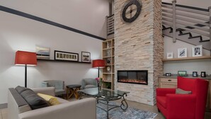 Uma sala de estar moderna com lareira, uma mesa de centro de vidro, uma poltrona vermelha e uma estante de livros.