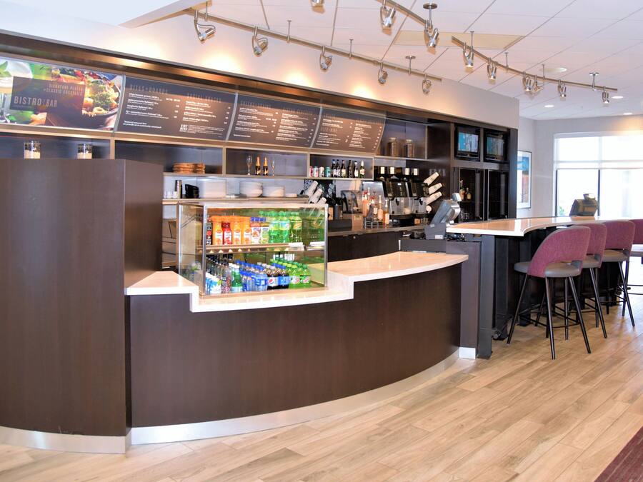 Uma área de bar moderna com balcão curvo, vitrine refrigerada e quadro de cardápio.