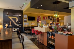 Uma área de bar com balcão, banquetas vermelhas e diversos garrafas e copos.