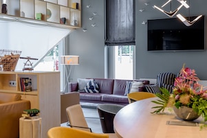 Uma sala de estar moderna com sofá, cadeiras, mesa e televisão.