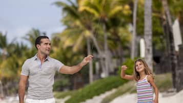 Um homem e uma menina em uma praia arenosa, com palmeiras ao fundo.