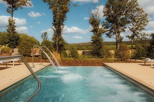 Piscina com cascata, cercada por árvores e céu claro.