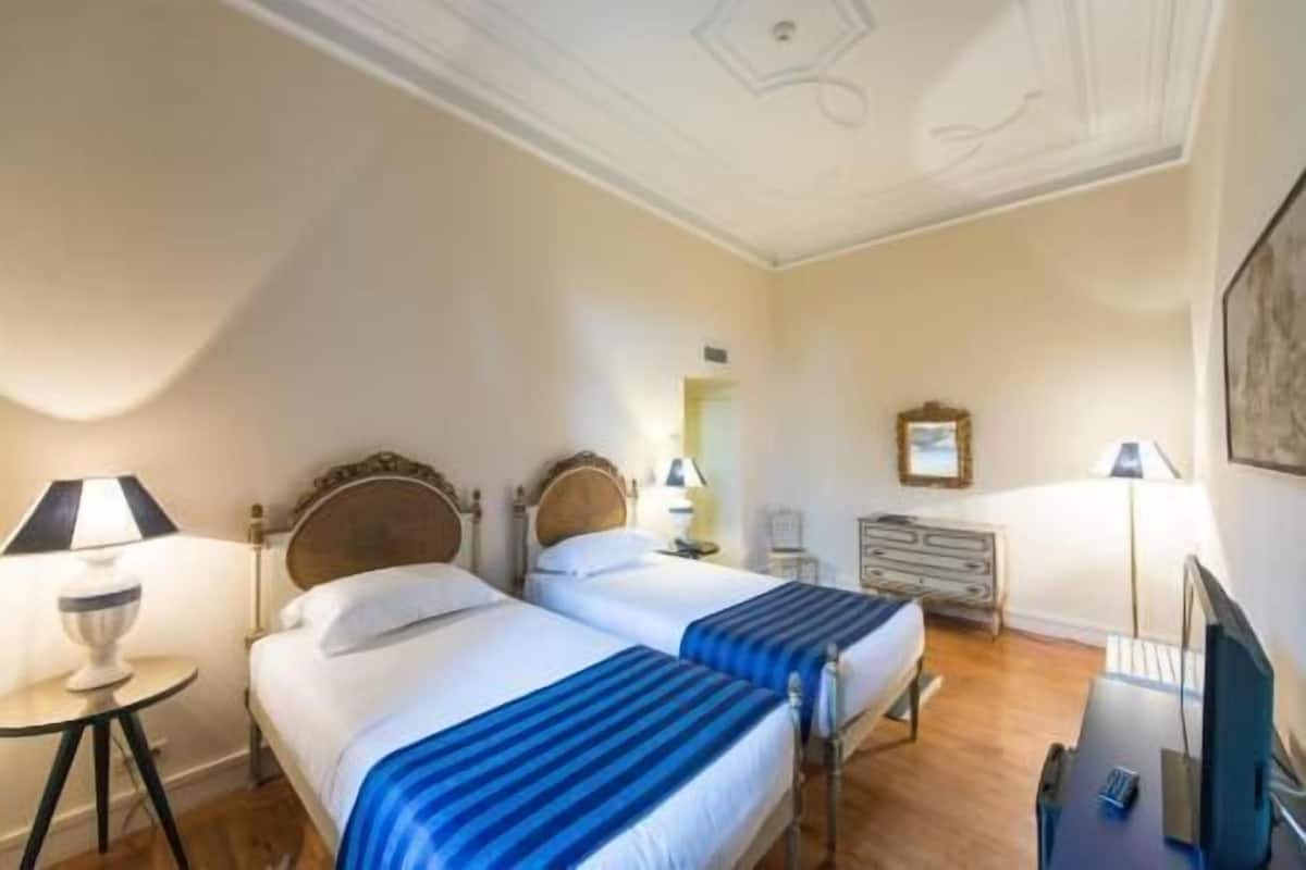 Quarto de hotel com duas camas, uma cômoda, uma escrivaninha e uma cadeira.