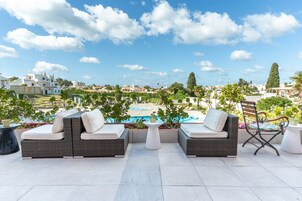 Terraço no telhado com móveis de vime, piscina e vista da cidade.