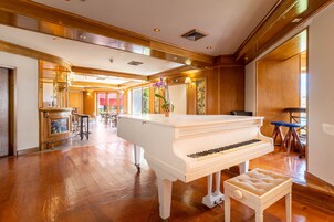 Um piano de cauda em uma sala ampla, com piso de madeira, área de bar e uma grande janela.