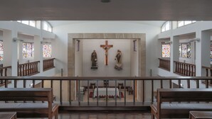 Interior de igreja com bancos, vitrais e uma cruz.
