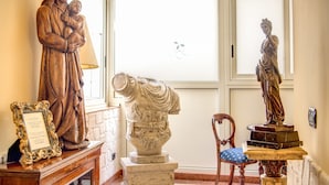Quarto com estátua de mulher segurando um bebê, busto, cadeira e quadro em cima de uma mesa.