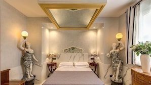 Quarto com uma cama grande, paredes de mármore e duas estátuas segurando luminárias.
